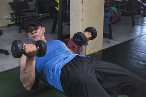 A Fit Asian Man In A Blue Tank Top Does Lying Dumbbell Curl On A Bench Challenging Bicep