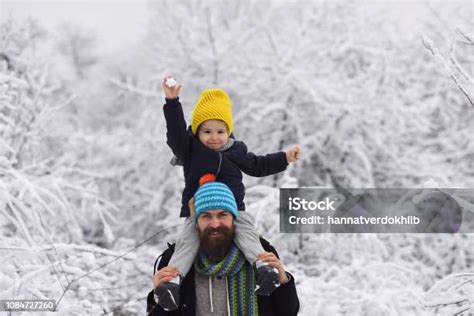 젊은 아버지와 아름 다운 작은 아들 겨울 숲에서 산책에 밝은 니트 모자에 수염 소년 남자 어깨에 앉아 위로 올린된 손을 눈덩이