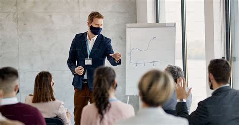 안면 마스크를 쓴 비즈니스 리더가 동료 그룹에게 프레젠테이션을 하는 동안 그 중 한 명이 손을 들어 무언가를 묻고 있습니다 사진 Unsplash의 사업 이미지