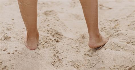 여자 엉덩이와 그을린 다리는 모래 해변 라이프 스타일을 배경으로 모래에 있습니다 스웨터와 수영복을 입은 세련된 젊은 여성이 해안에서 휴식을 취하고 있는 모래 엉덩이를