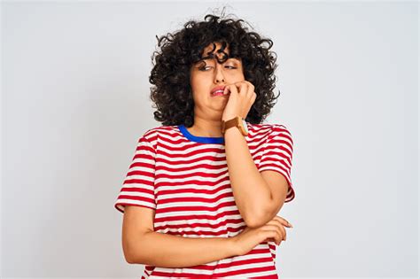 곱슬 머리를 가진 젊은 아랍 여자 는 고립 된 흰색 배경 위에 줄무늬 티셔츠를 입고 스트레스와 긴장 한 입물기 손톱에 손을 불안 문제 T 셔츠에 대한 스톡 사진 및 기타