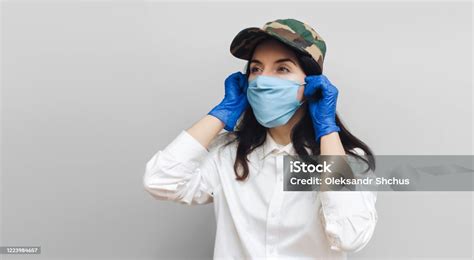 흰색 스모크 위장 모자를 쓴 한 여성 군인 의료진이 회색 배경에 파란색 보호 마스크를 착용하거나 벗습니다 육군 검역의 개념