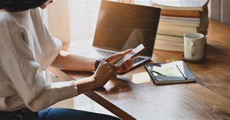 컴퓨터 노트북 커피 컵 책 더미 질서 정연한 도서관의 노트북 앞에 있는 나무 테이블에 앉아 스마트폰을 손에 들고 있는 아름다운 여성의 사진 사진 Unsplash의