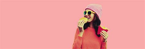 분홍색 배경에 모자를 쓰고 햄버거와 감자 튀김 패스트 푸드를 가진 세련된 행복한 미소를 짓는 젊은 여성의 초상화 20 29세에 대한 스톡 사진 및 기타 이미지 Istock