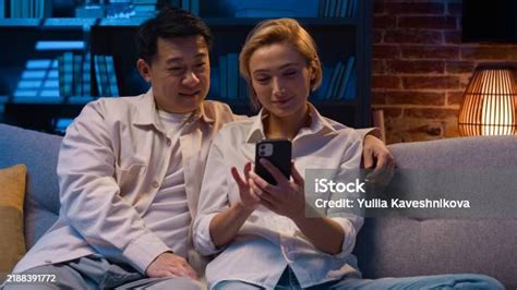 가족 다인종 커플 아시아 남성과 백인 여성 밤 집에서 물건 구매 인터넷 스토어 휴대 전화 온라인 쇼핑 스마트 폰으로 함께 검색 이야기 토론 주문 음식 배달 2명에 대한 스톡
