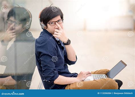 Young Asian Man Pushing Glasses Up On Nose While Using Laptop Stock