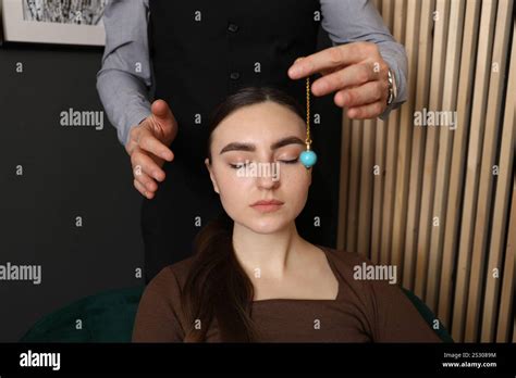 Psychologist using pendulum while working with patient during hypnosis session indoors, closeup ...