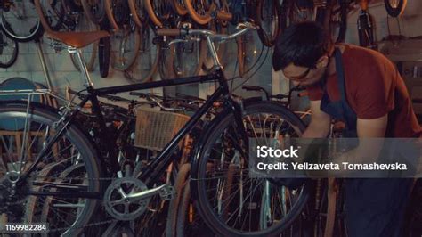 테마 중소 기업 자전거 수리 보호 안경 장갑과 Fartuhe에 젊은 갈색 머리 백인 남자는 수리 및 차고 작업장에서 림 브레이크와 바퀴 회전 자전거를 튜닝하기 위해 손