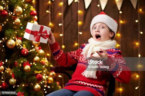 메리 크리스마스와 해피 홀리데이 메리 크리스마스와 해피 홀리데이를 입고 조명 장식 크리스마스 나무 근처 실내 앉아 선물 상자와 쾌활한 산타 도우미 소녀 가정 생활에 대한