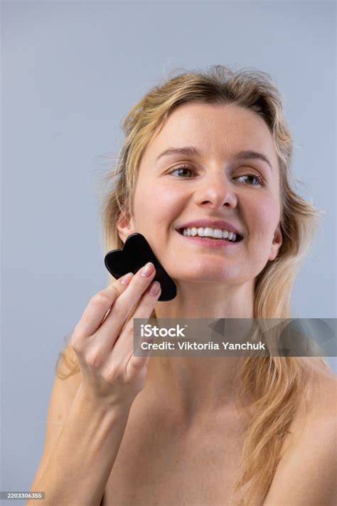 블랙 괄사 도구를 사용하여 얼굴 미용 루틴을 향상시키고 빛나는 피부와 휴식을 위한 자기 관리 및 웰빙 관행을 강조하는 미소 짓는 여성 괄사에 대한 스톡 사진 및 기타 이미지