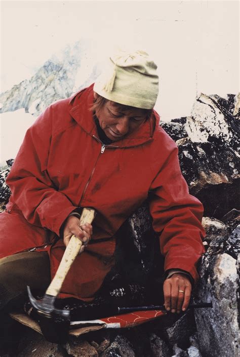 A Woman In A Red Jacket And White Toque Sits Leaned Up Against The Rock While Wielding A Hammer