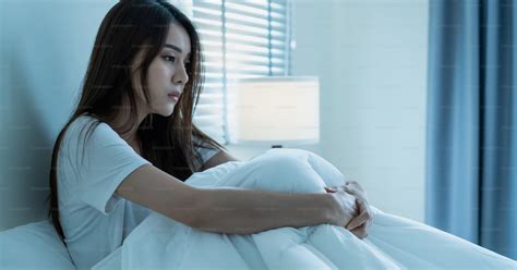아시아의 아름다운 화가 우울한 소녀가 침실의 침대에 혼자 앉아 있습니다 매력적인 불행한 젊은 여성은 삶의 문제로 외롭고 화가 나서 집에서 어두운 밤 방에서 자신을 다치게