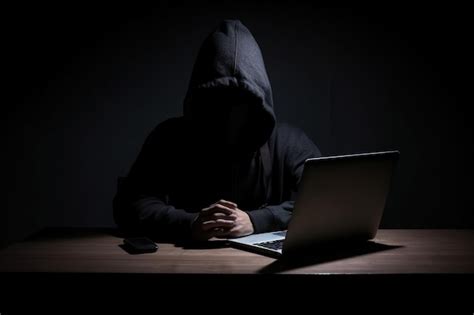 Premium Ai Image Hacker Wearing Black Hoodie Using Laptop Computer While Working On Dark