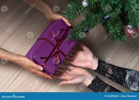 Close Up Of The Hands Of Two Women Passing A Christmas Present To Each