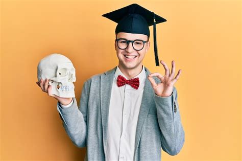 Premium Photo Young Caucasian Nerd Man Wearing Glasses And Graduation Cap Holding Skull Doing