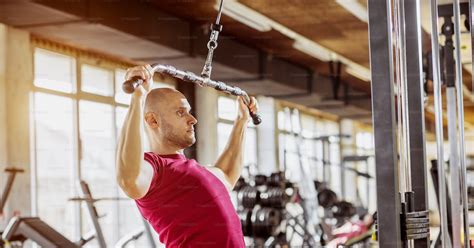 동기 부여되고 집중된 강한 근육질의 스포티 한 피트니스 젊은 대머리 남자가 벤치에 앉아 체육관에서 등 근육을 위해 기계에서 금속