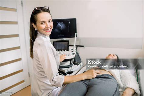 병원에서 여성 환자 복부의 초음파 검사를 실시하는 동안 초음파 기계를 사용하여 젊은 웃는 여자 의사 초음파 검사기 2명에 대한