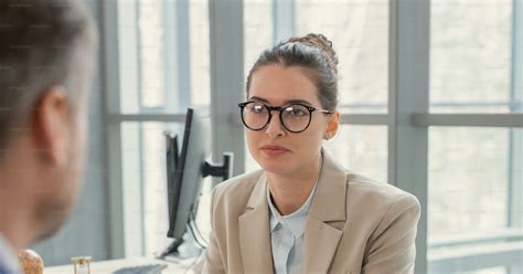 안경을 쓴 자신감 넘치는 여성이 테이블에 앉아 펜을 들고 회의에서 동료들의 말을 듣고 있다 사진 Unsplash의 양복 이미지