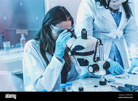 Young Female Scientist In Lab Coat And Safety Goggles Examining A