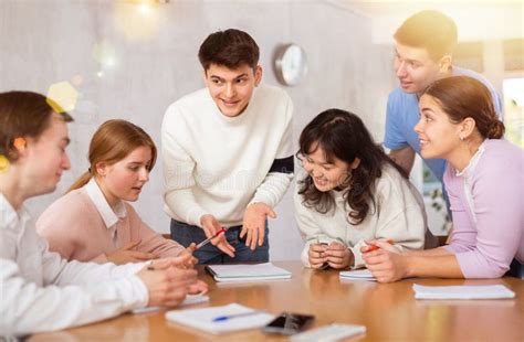 Young Teacher Discussing His Notes With Students Around The Table Stock Young Teacher Discussing His Notes With Students Around The Table Stock