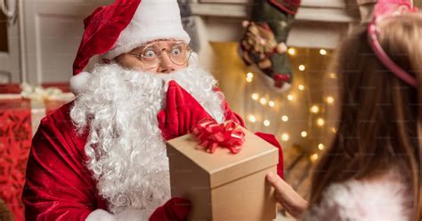 당신은 이 선물을 받을 자격이 있습니다 여자 아이에게 상자를 주는 흥분된 산타클로스의 초상화 그는 빨간 의상을 입고 편안한 안락 의자에 앉아있다 사진