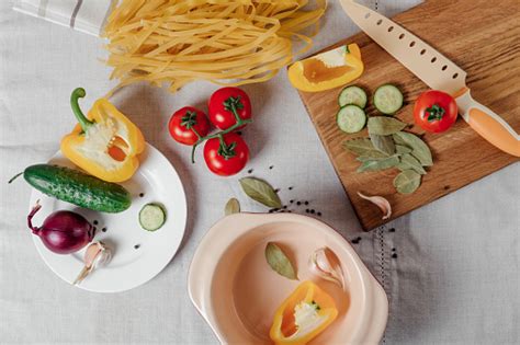 테이블에 야채와 원시 파스타 체리 토마토 노란 피망 오이 붉은 양파와 마늘이 칼을 들고 도마위에 올려보냅니다 요리용 재료 개념에