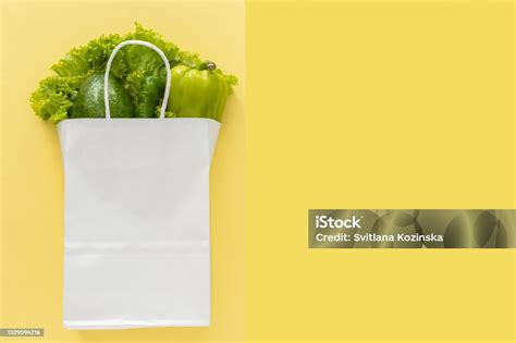 배달 건강 한 음식 배경 노란색 배경에 흰색 종이 가방 야채비건 채식 요리 식료품 쇼핑 식품 슈퍼마켓과 깨끗한 식사 개념 맨 위 보기입니다 텍스트 배치 가방에 대한 스톡