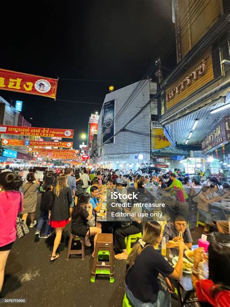 태국 방콕 차이나타운의 야간에 야외 식사를 하는 길거리 음식 시장의 클로즈업 이미지 길거리 음식 가판대 주변의 의자에 앉아 있는 사람들 빨간 거리 배너 전경에 초점 건물