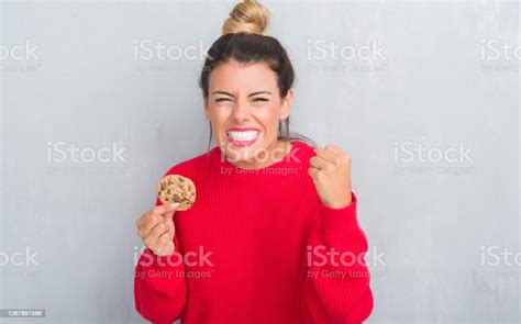 회색 그런 지 위에 젊은 성인 여자 벽 화가 초콜릿 칩 쿠키 먹고 미친과 제기 손으로 소리 분노와 좌절 외치고 분노 개념 갈색 머리에 대한 스톡 사진 및 기타 이미지
