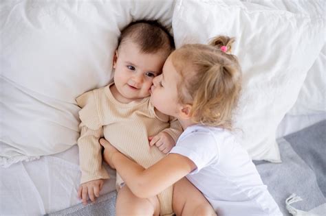 Premium Photo Older Sister Baby Kisses And Hugs Baby At Home On The