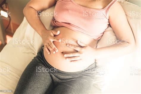 임신 한 여자는 그녀의 아이를 돌보는 동안 집에서 행복을 느낀다 임신 한 배에 아기를 들고 젊은 기대 어머니 출산 전 관리 및 여성 임신 개념 가족에 대한 스톡 사진 및