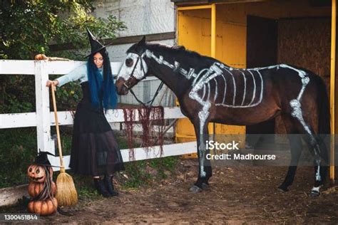 마녀로 옷을 입은 소녀가 산호 울타리 옆에 서 있고 그 옆에 는 그려진 해골을 가진 말이 서 있습니다 25 29세에 대한 스톡 사진 및 기타 이미지 Istock