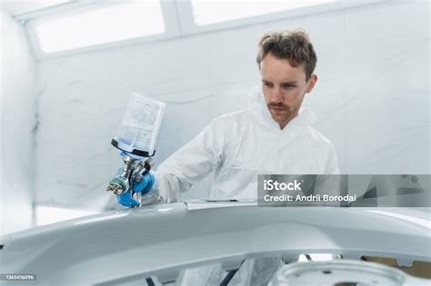 젊은 곱슬 자동차 화가는 자동차 범퍼를 바니시합니다 남자는 스프레이 부스에서 작동합니다 차 체체 부품을 페인팅하는 과정 25 29세에 대한 스톡 사진 및 기타 이미지