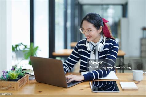 컴퓨터를 사용하고 헤드폰을 착용하고 노트북을 사용하여 도서관의 나무 책상에서 화상 회의를 통해 온라인으로 공부하는 십대 아시아 여성의 초상화 개념에 대한 스톡 사진 및 기타