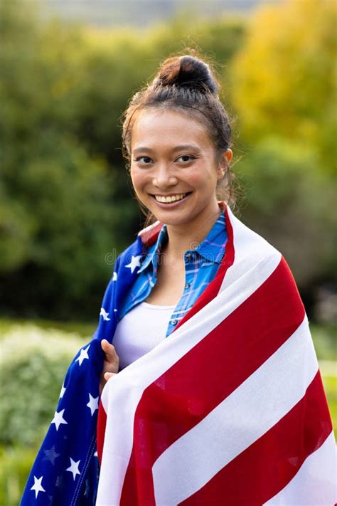 Portrait Of Happy Asian Woman Covered With Flag Of Usa In Garden Stock