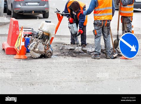 Road Workers In Reflective Clothing On A Fenced In Section Of Road Repairing The Roadway Using A