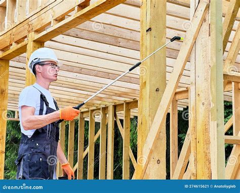 Worker Applying Fire Retardant Using Sprayer While Constructing Wooden Frame House Near Forest