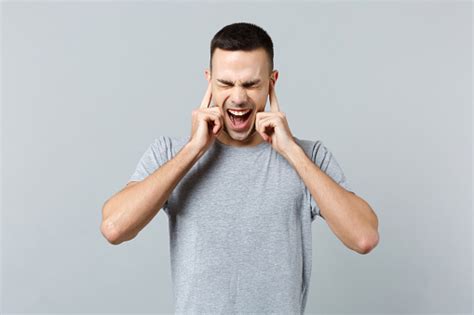 스튜디오에서 회색 배경에 고립 된 손가락으로 귀를 덮고 눈을 닫은 유지 캐주얼 옷에 젊은 남자를 좌절 비명 사람들은 진심으로