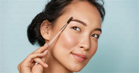 아름다움 웃는 여자는 메이크업 브러쉬 클로즈업으로 눈썹을 닦는다 아름다운 행복한 아시아 소녀 모델의 초상화는 메이크업을 하고