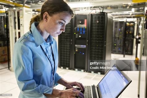 Caucasian Woman Technician Running Diagnostics On Computer Servers In A Server Farm High Res