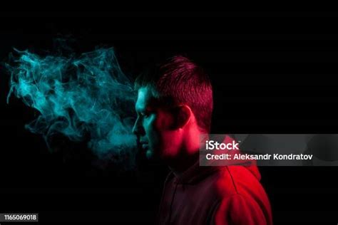 성인 심각한 남자의 얼굴의 초상화를 닫아 녹색 독성 연기를 내뿜고 전자 담배를 피우고 검은 배경에 파란색과 빨간색 으로 빛나는