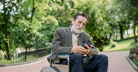 수염 난 백인 노인은 공원에서 혼자 휠체어에 앉아 스마트 폰을 사용하여 인터넷이나 Socail 네트워크를 사용하고 있습니다 사진 Unsplash의 가로 이미지