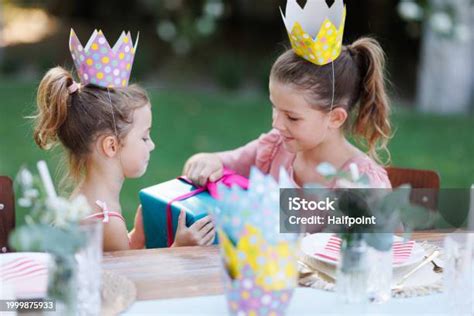 정원에서 야외에서 생일 파티를 하는 작은 친구들 생일 선물을 여는 종이 왕관을 가진 귀여운 소녀들 어린이를 위한 생일 가든 파티
