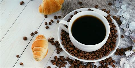 커피 원두와 빈티지 나무 테이블에 크루아상을 곁들인 커피 한 잔 홈메이드 크루아상과 블랙 커피 또는 아메리카노가 함께 제공됩니다 맛있는 크루아상과 함께 커피 휴식 가을 구성