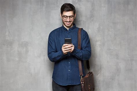 데님 셔츠를 입고 유럽 남자를 웃 고 손에서 전화를 통해 서 서 또는 메시지를 교환 질감 된 벽 배경에 고립 가방에 대한 스톡 사진 및 기타 이미지 Istock
