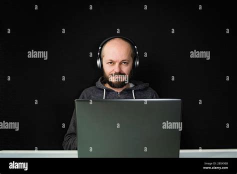 Caucasian Man In Hoodie And Headphones Sitting Behind The Laptop And Working Black Background