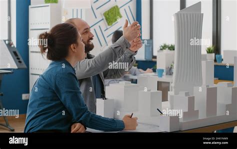 Architects Using Smartphone To Design Construction Layout With Building Model And Blueprints