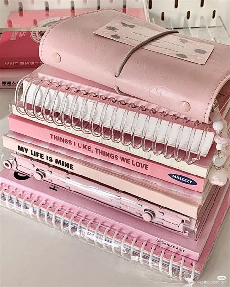 A Stack Of Pink Notebooks Sitting On Top Of A White Table Next To A Pile Of Books