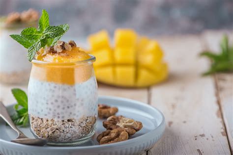 시리얼과 망고 및 키 위의 퓌 레와 호두 유리 항아리에 민트로 만든 치아 씨앗과 아몬드 밀크의 홈메이드 푸딩 소박한 나무