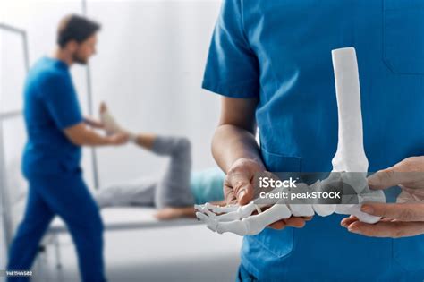 외상 및 정형외과에서 환자의 부상당한 다리를 조수 검사하는 동안 해부학적 발 골격 모델을 보여주는 족부 전문의 발목에 대한 스톡